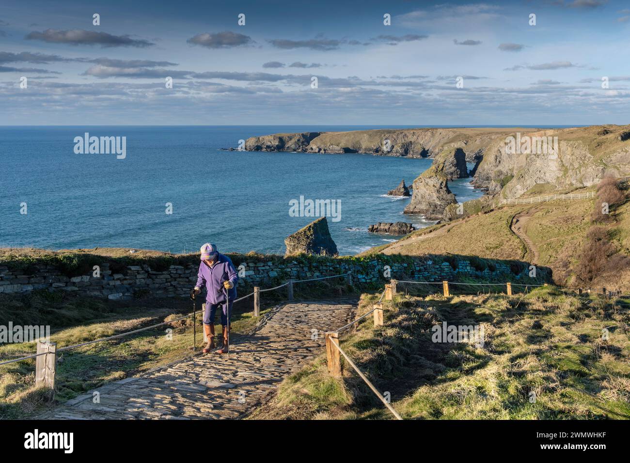 A mature woman using walking poles to help her to walk up a footpath ...