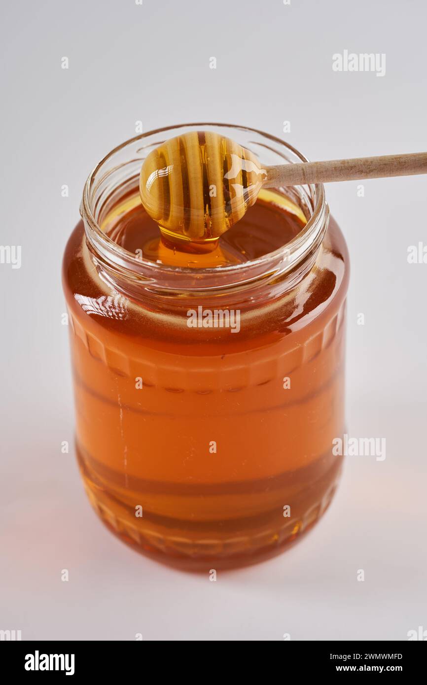 A jar with golden bee honey and a dipping stick isolated on white ...