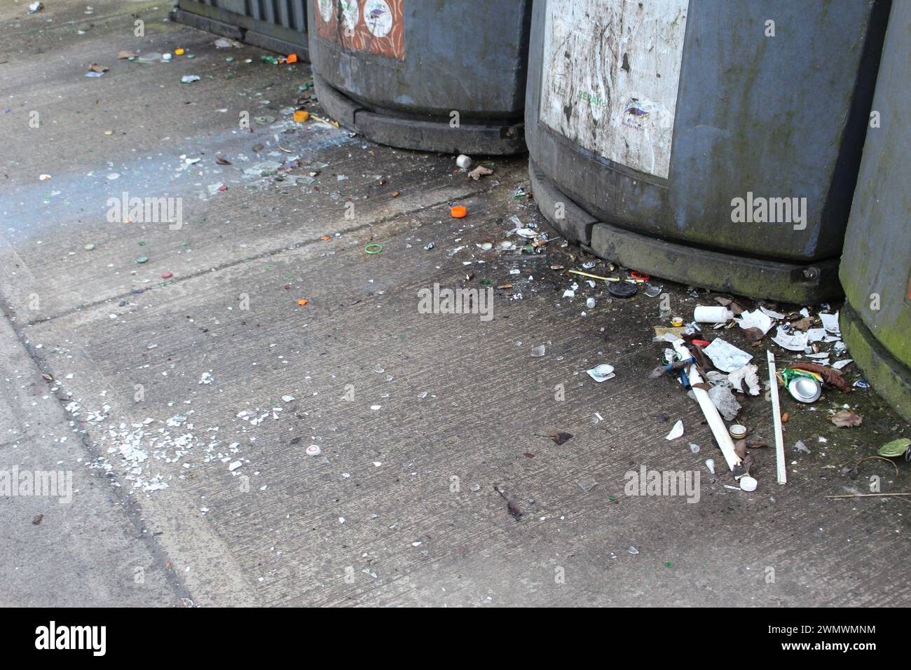 Litter overflow outside of a municipal waste area with recycling and garbage cans seen across ...