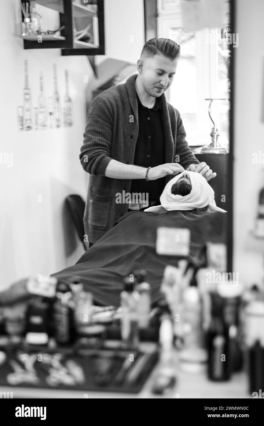 The barber covers the clients face with a hot wet towel to steam off ...