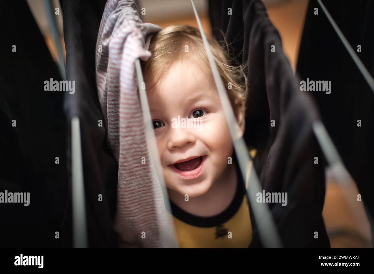 Smiling playful baby boy is hiding between clothes it dries up. Happy ...
