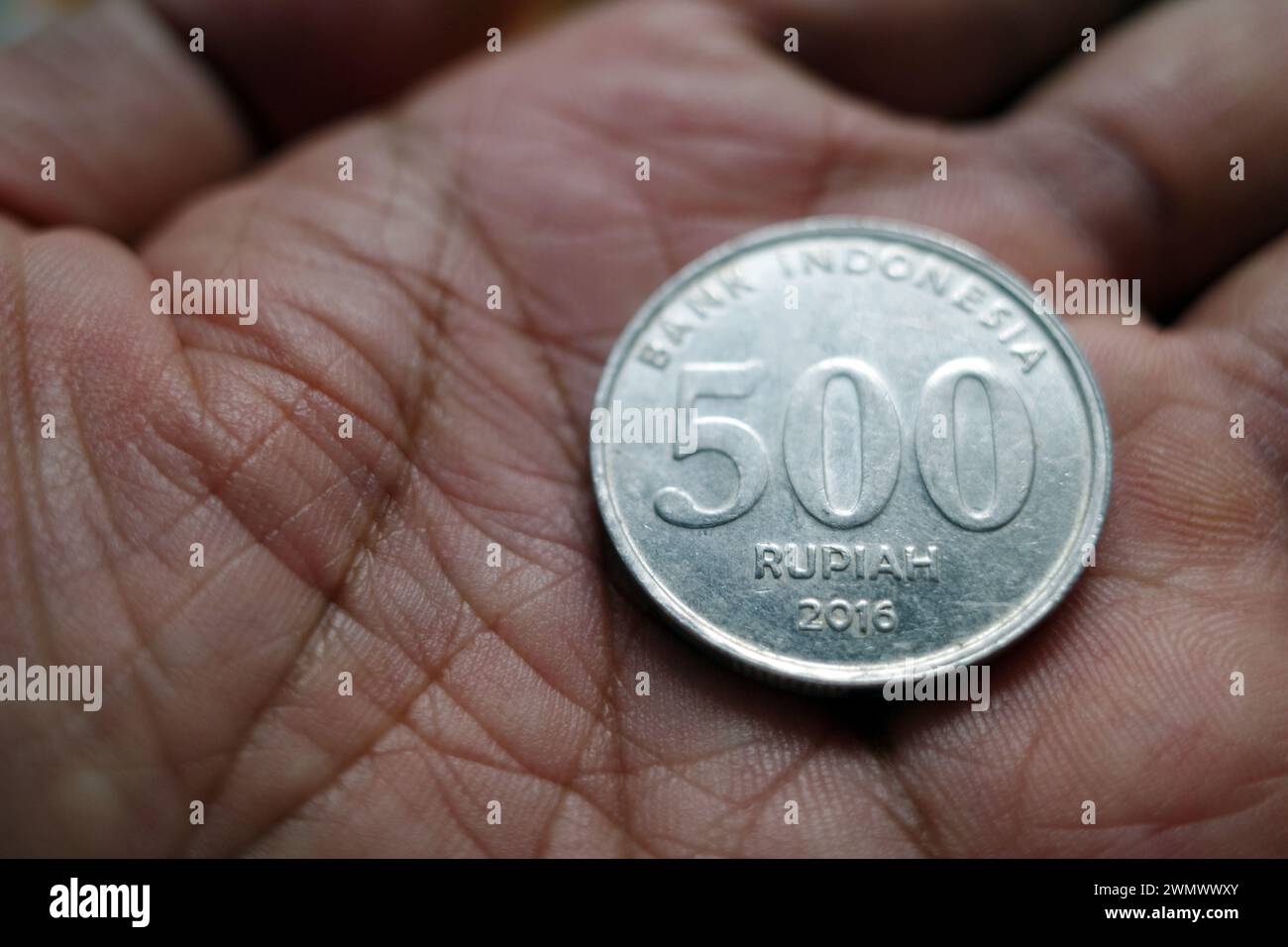 An Asian man holds Indonesian coin money, 500 Rupiah, in shallow focus ...