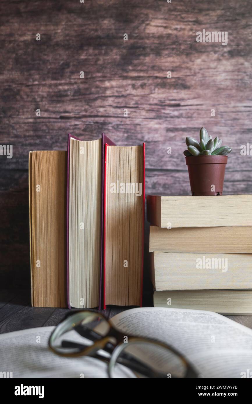 Open book, glasses on top in foreground, piles of books in background ...