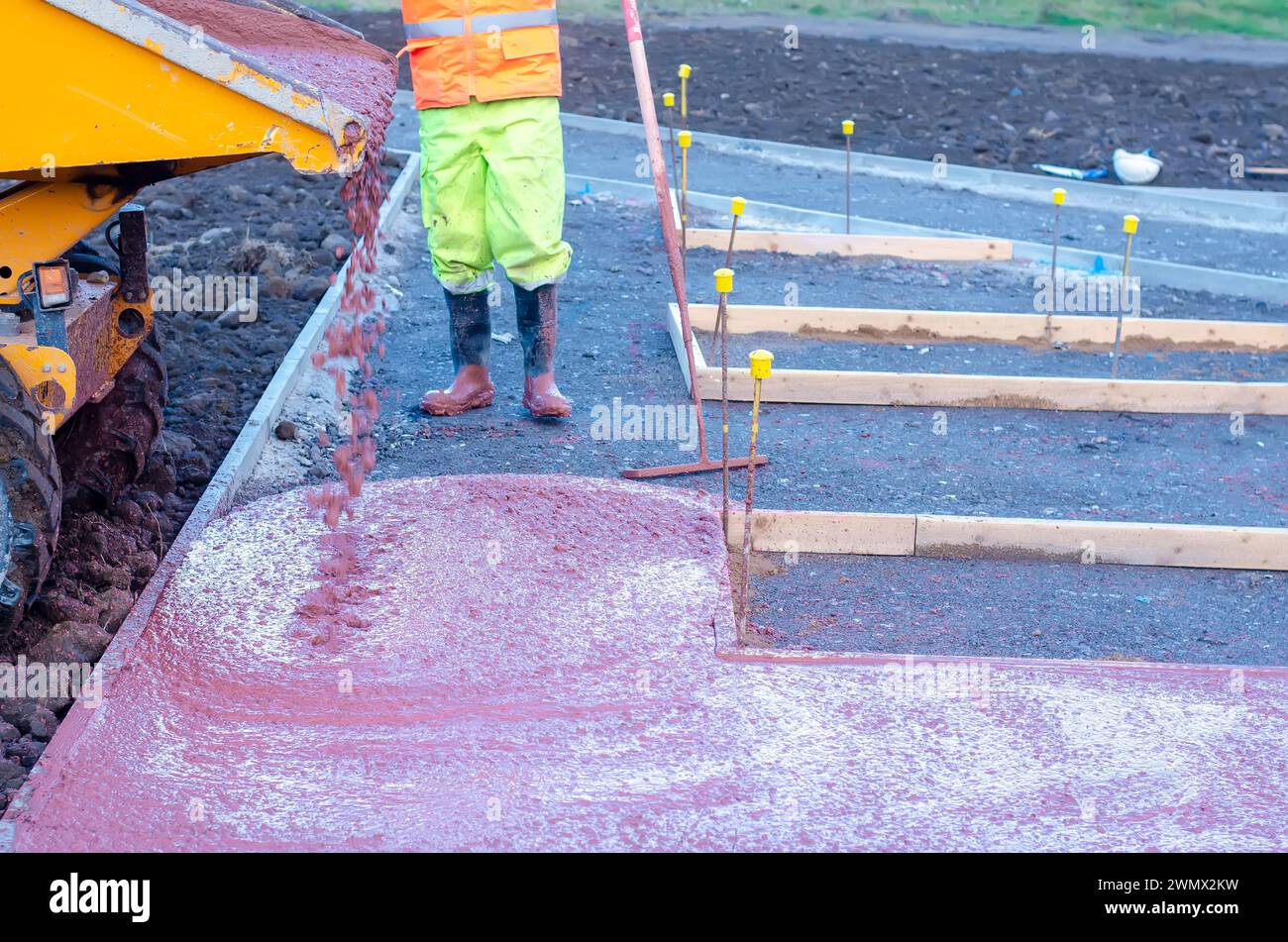 Builders pouring and levelling wet ready-mix concrete into formwork ...