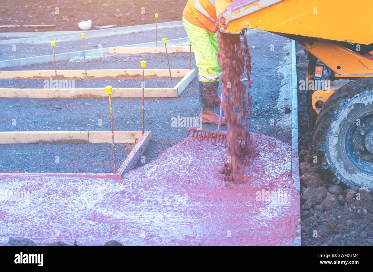 Builders pouring and levelling wet ready-mix concrete into formwork ...