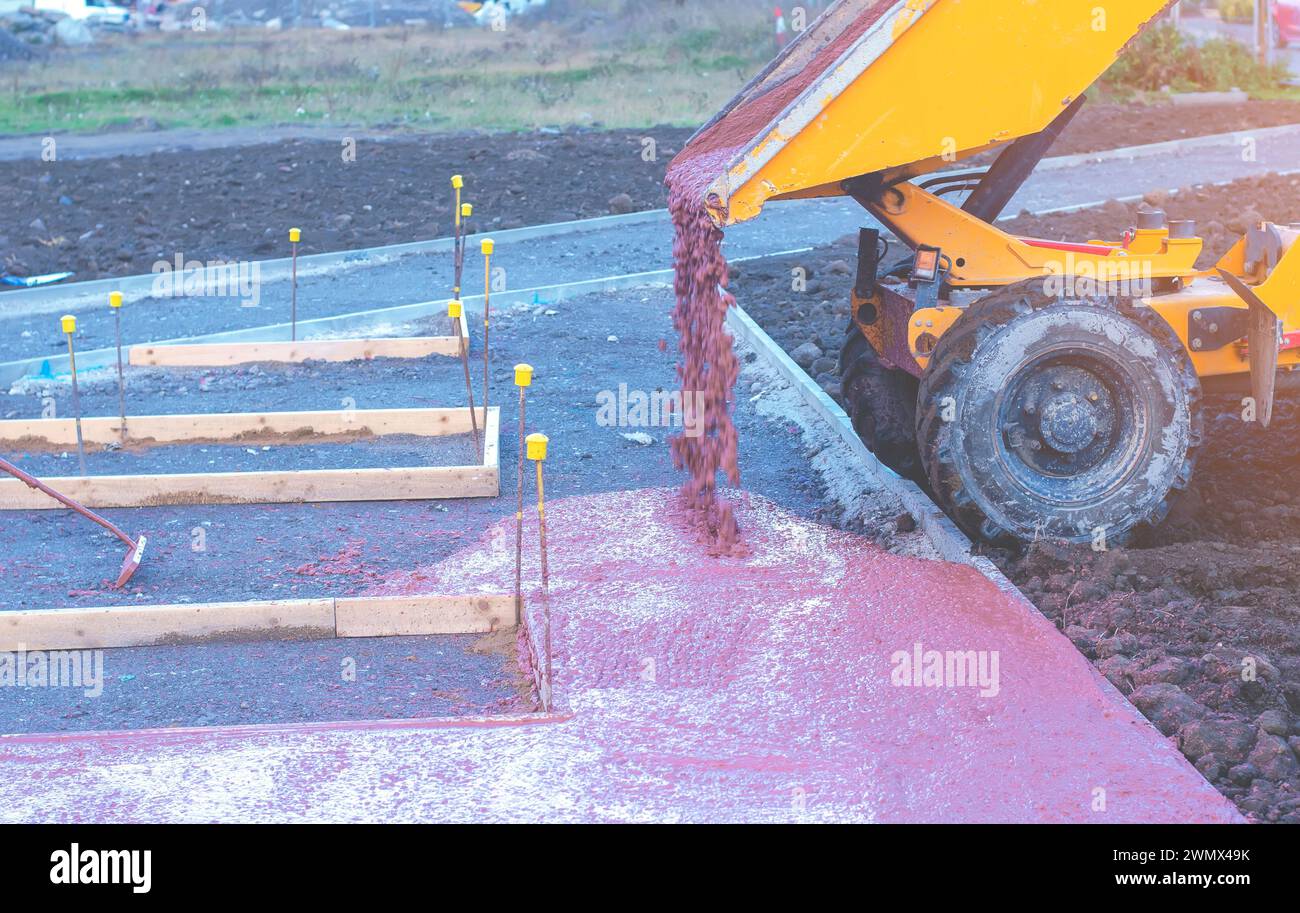 Builders pouring and levelling wet ready-mix concrete into formwork ...