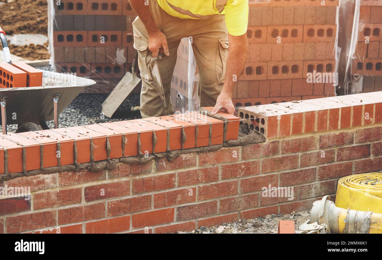 Industrial bricklayer laying bricks on cement mix on construction site ...