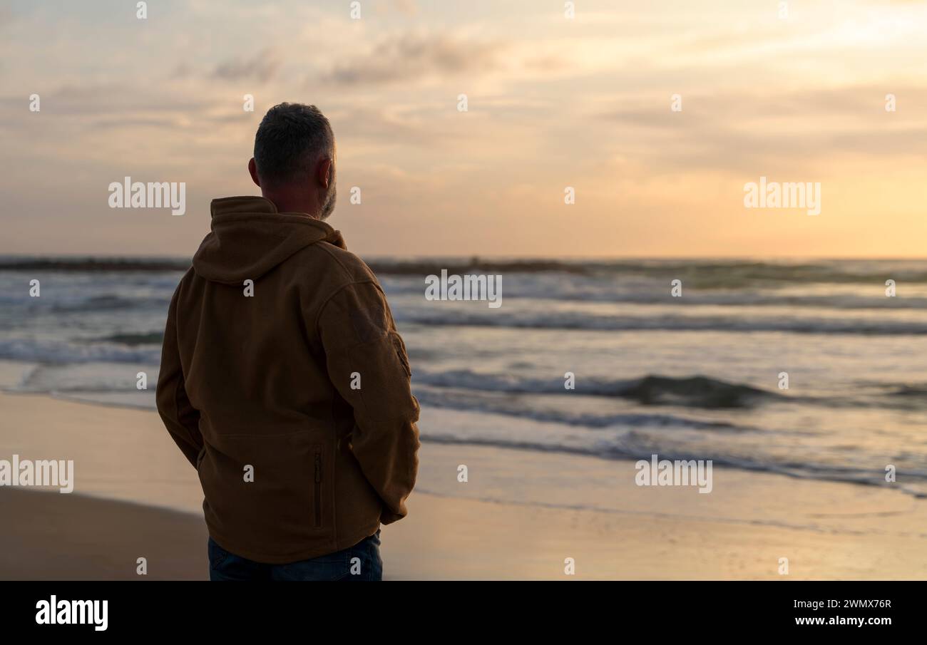 Bearded Man relaxing alone on the seaside on hot sunny day at sunset ...