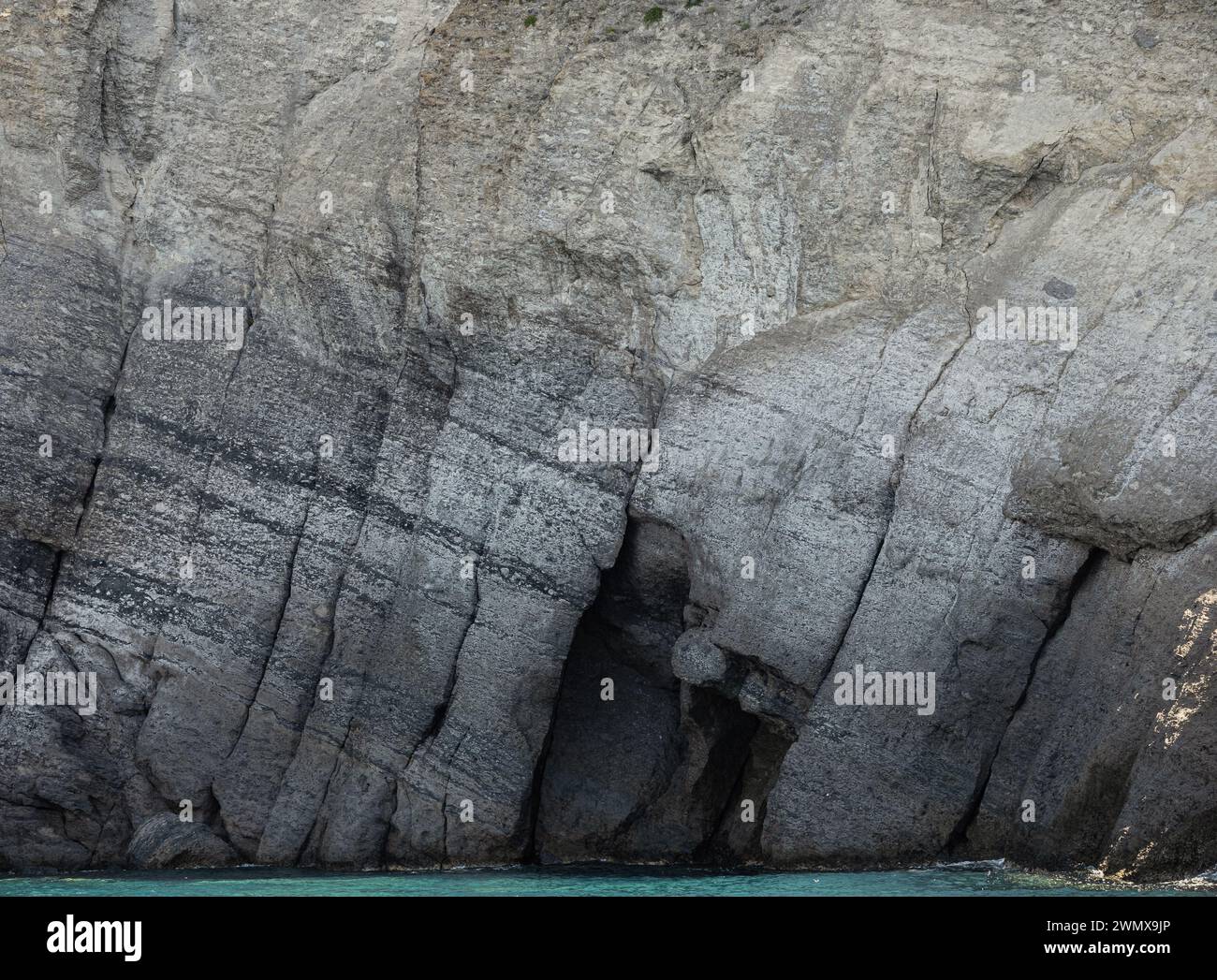 Weathered seaside rock face texture with blue water. Aged volcanic ...