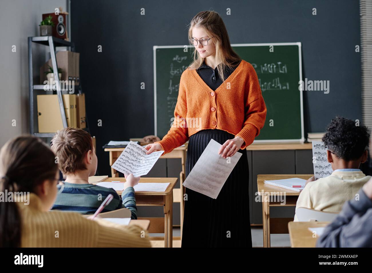 Medium long shot of young Caucasian teacher handing out sheet music to ...