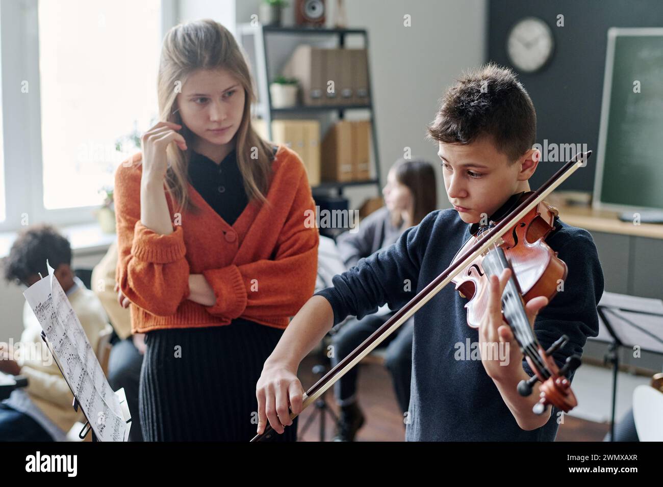Young Caucasian female teacher listening to her student playing violin ...