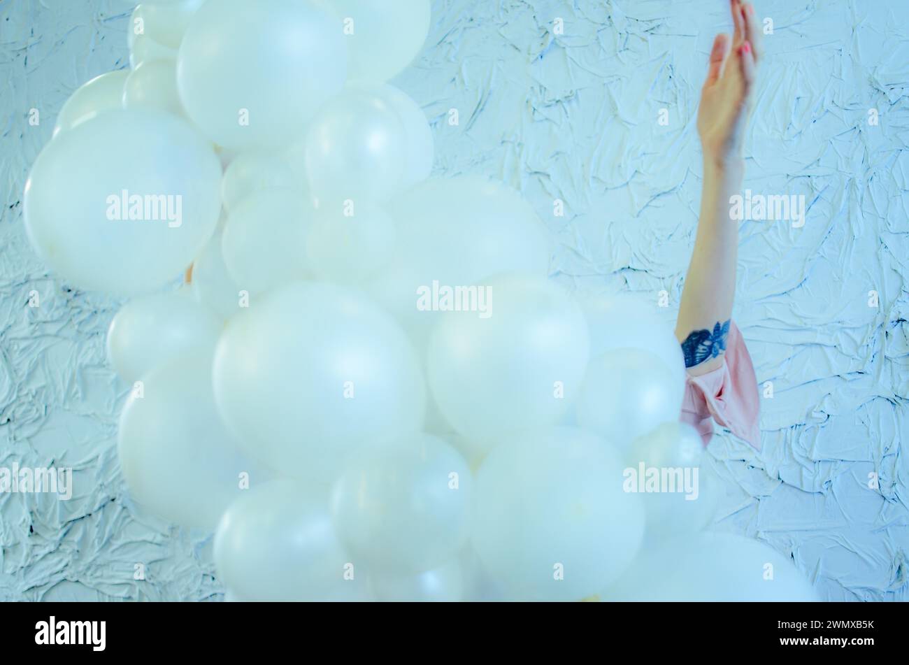 A close-up of an arm reaching for pastel balloons against a textured ...