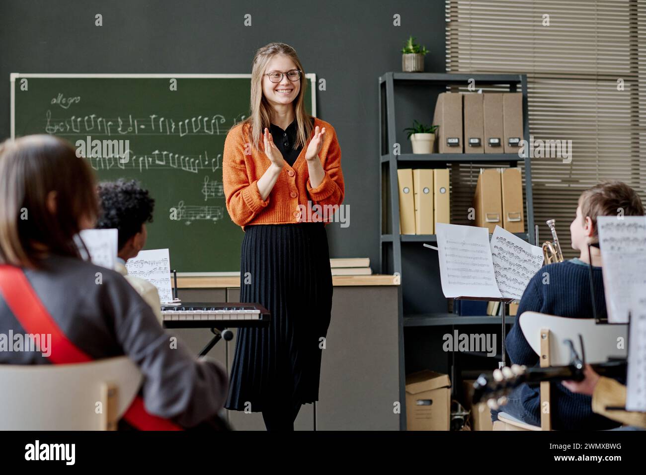 Cheerful young music teacher standing in front of her students in ...