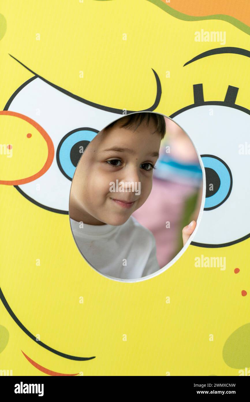 A young boy peers through a hole in the cheek of a Spongebob face ...