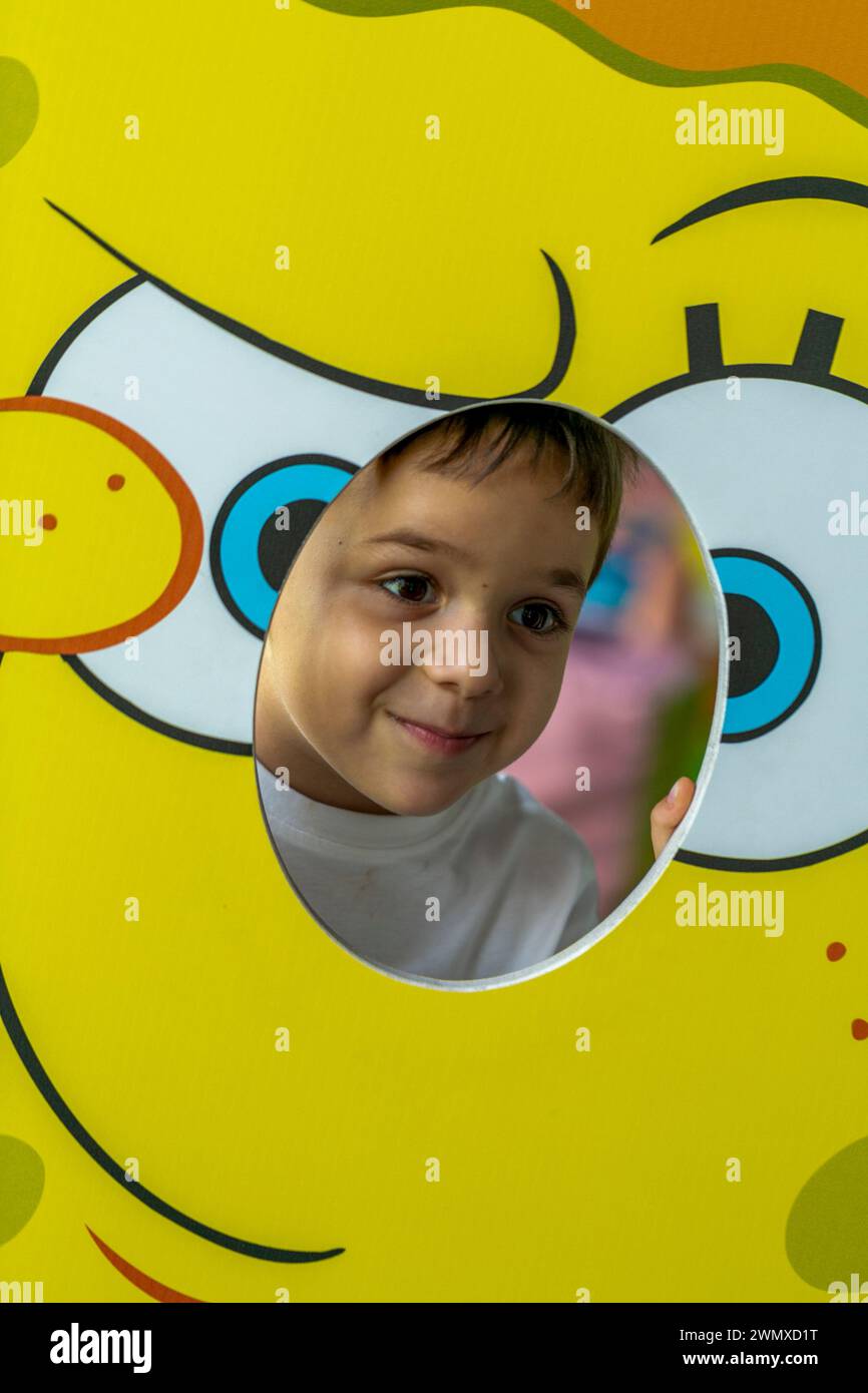 A young boy peers through a hole in the cheek of a Spongebob face ...