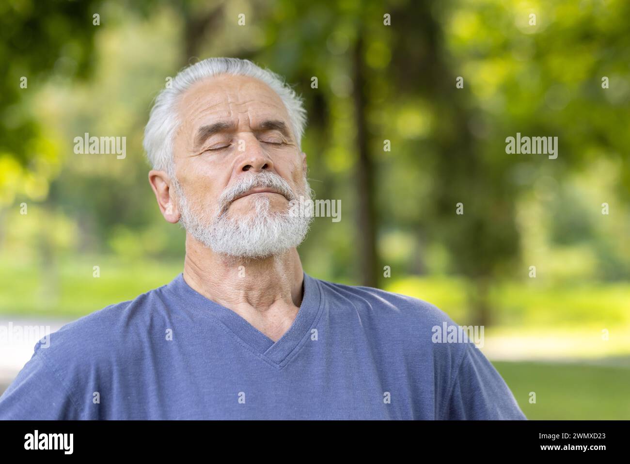 A gray-haired elderly man relaxes with closed eyes, taking a deep ...