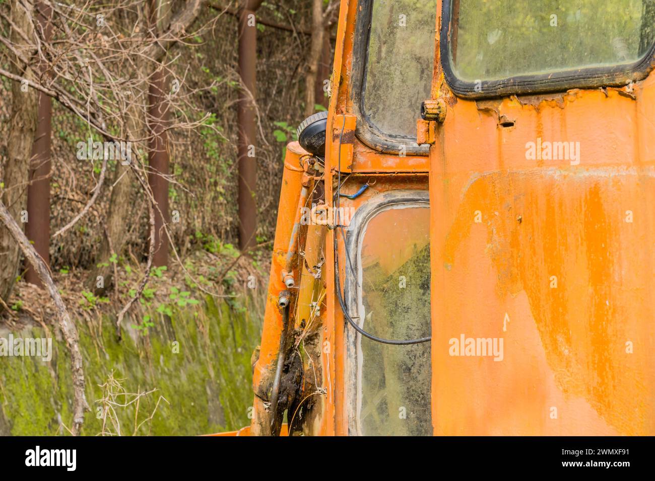 Detail of an old, rusty, abandoned orange vehicle with moss and nature ...