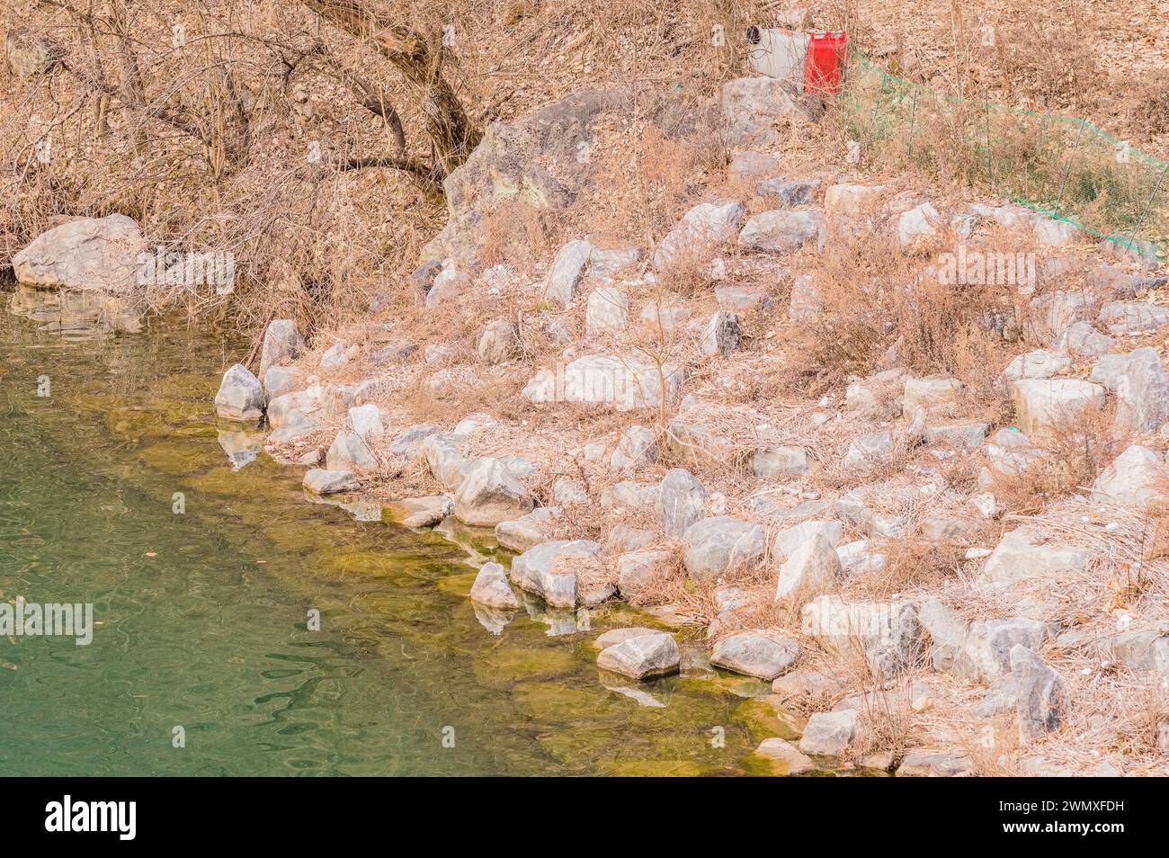 Clear water by a rocky shoreline with a red trash bin to one side, In ...