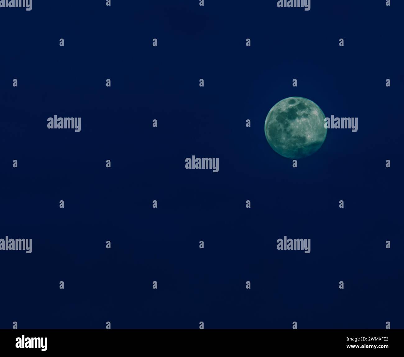 Full moon with details of craters and bright spots in a blue sky during ...