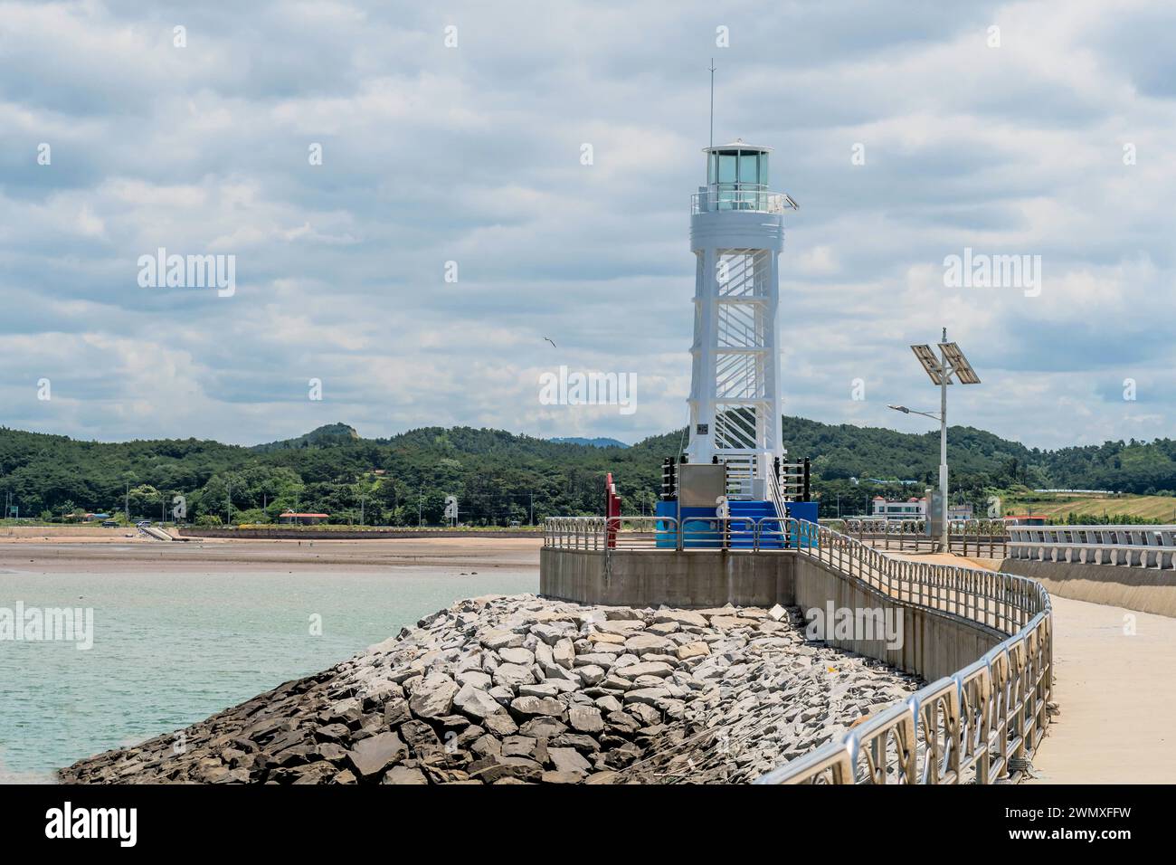 White lighthouse on end of pier under cloudy sky with beach in ...
