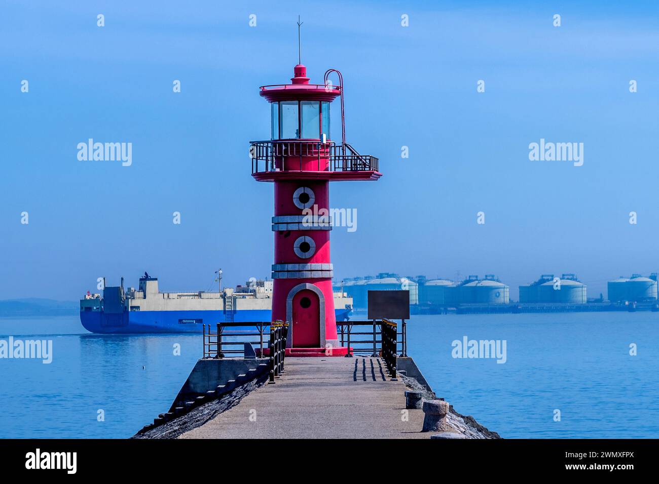 Large ocean cargo barge passing behind red lighthouse at end of ...