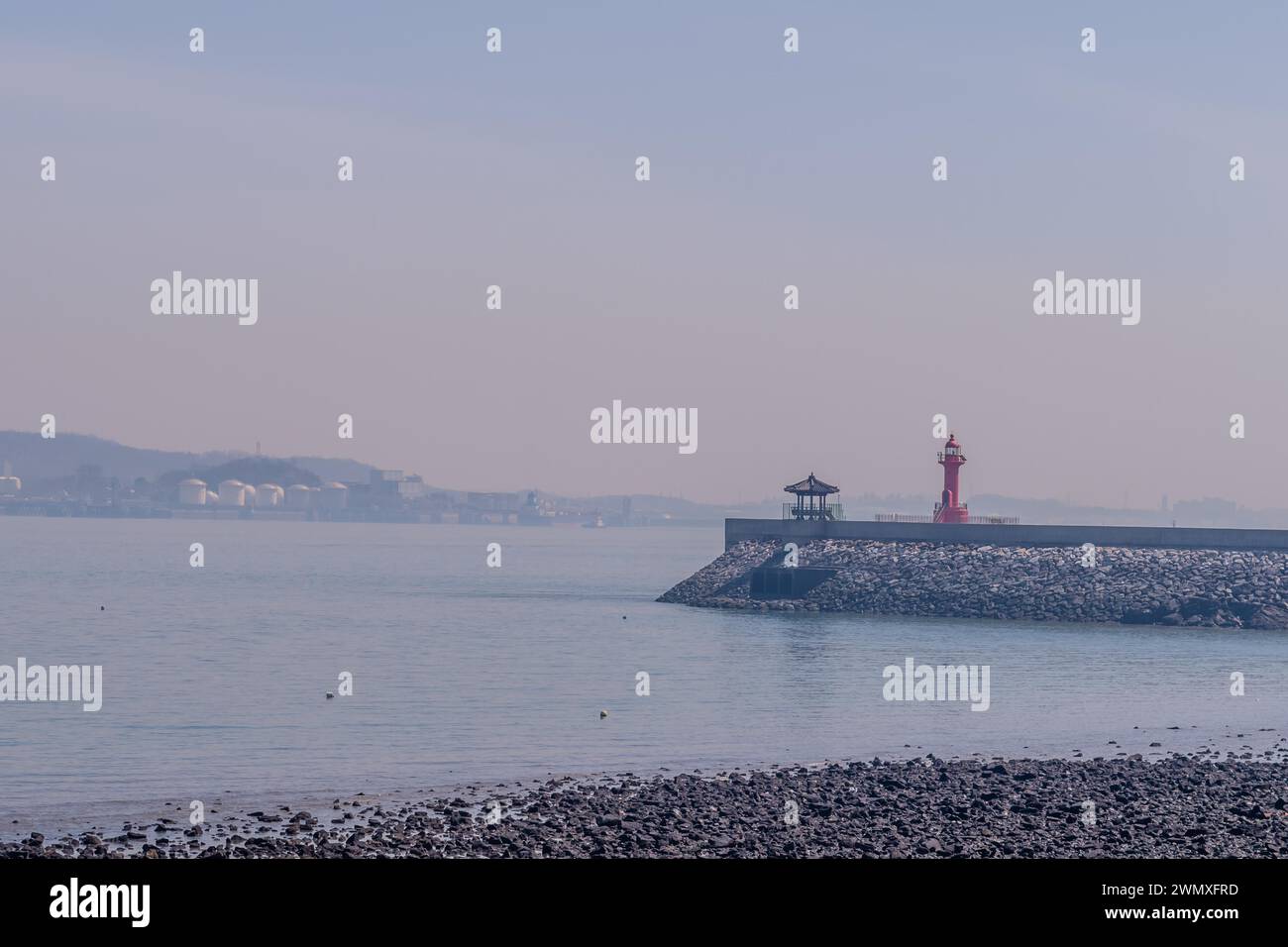 Red lighthouse at end of concrete and stone pier beside wooden gazebo ...