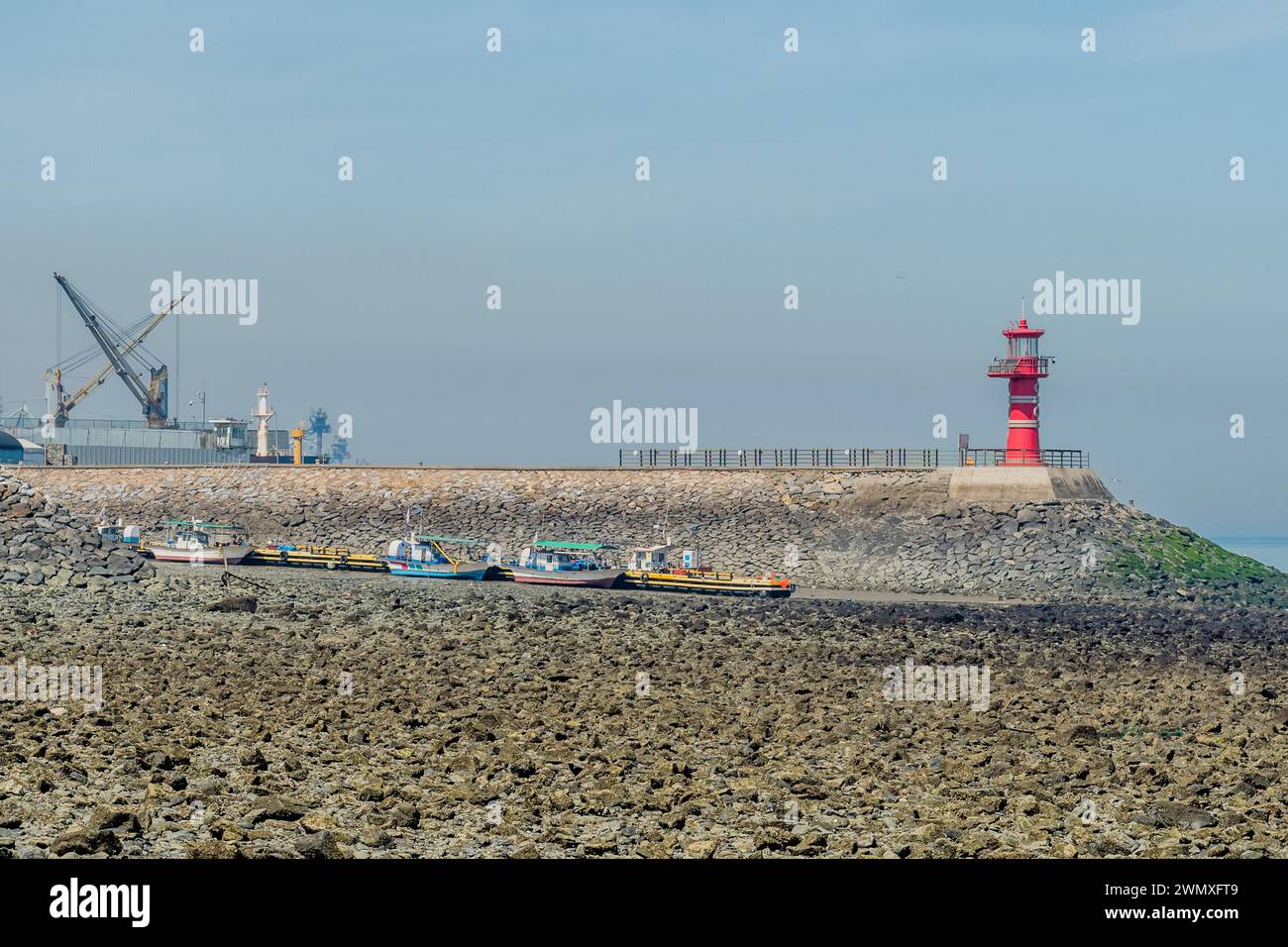 Fishing boats next on rocky shore at low tide beside pier and red ...