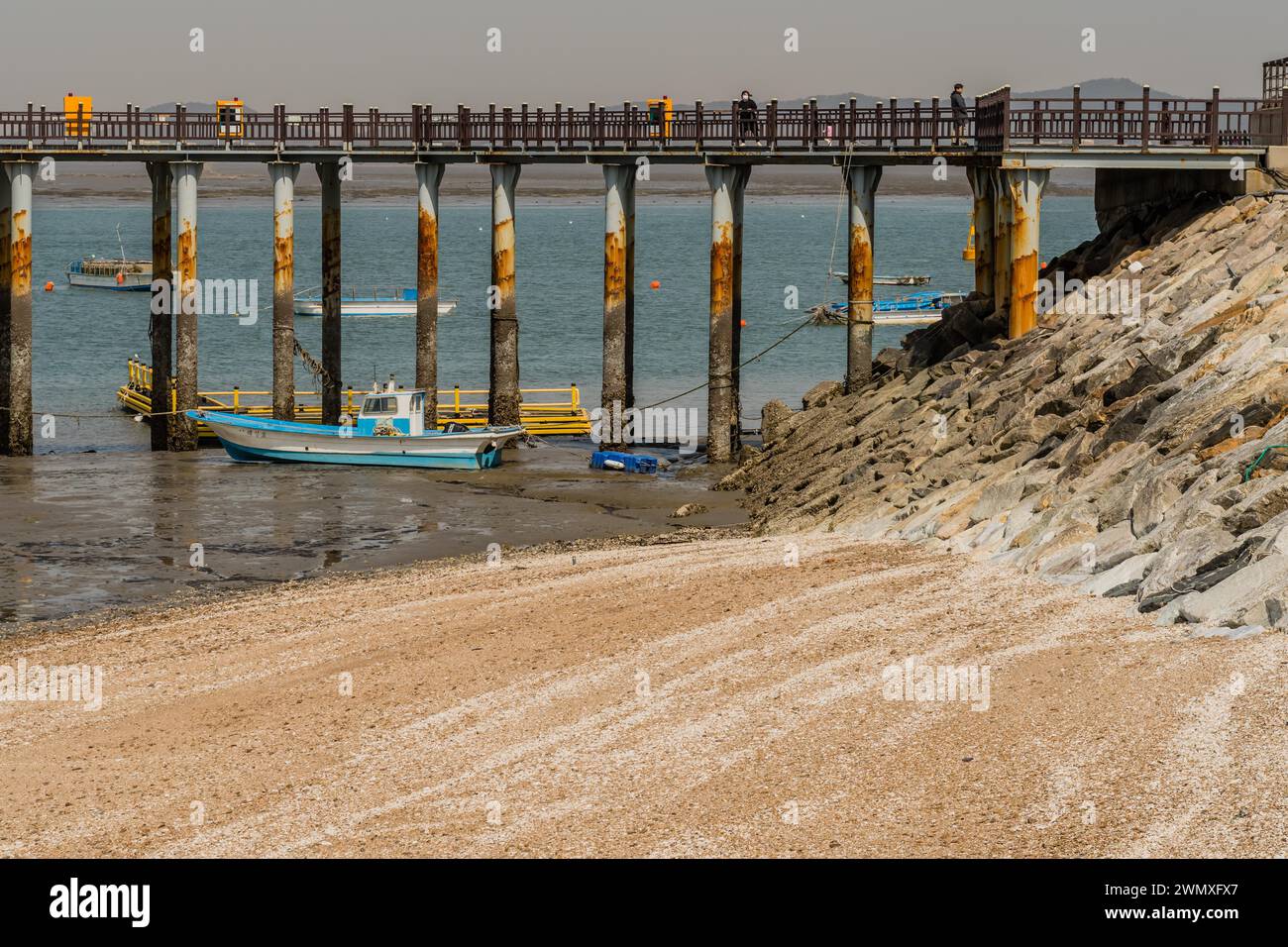 Small fishing trawler moored to pier support column at low tide in ...