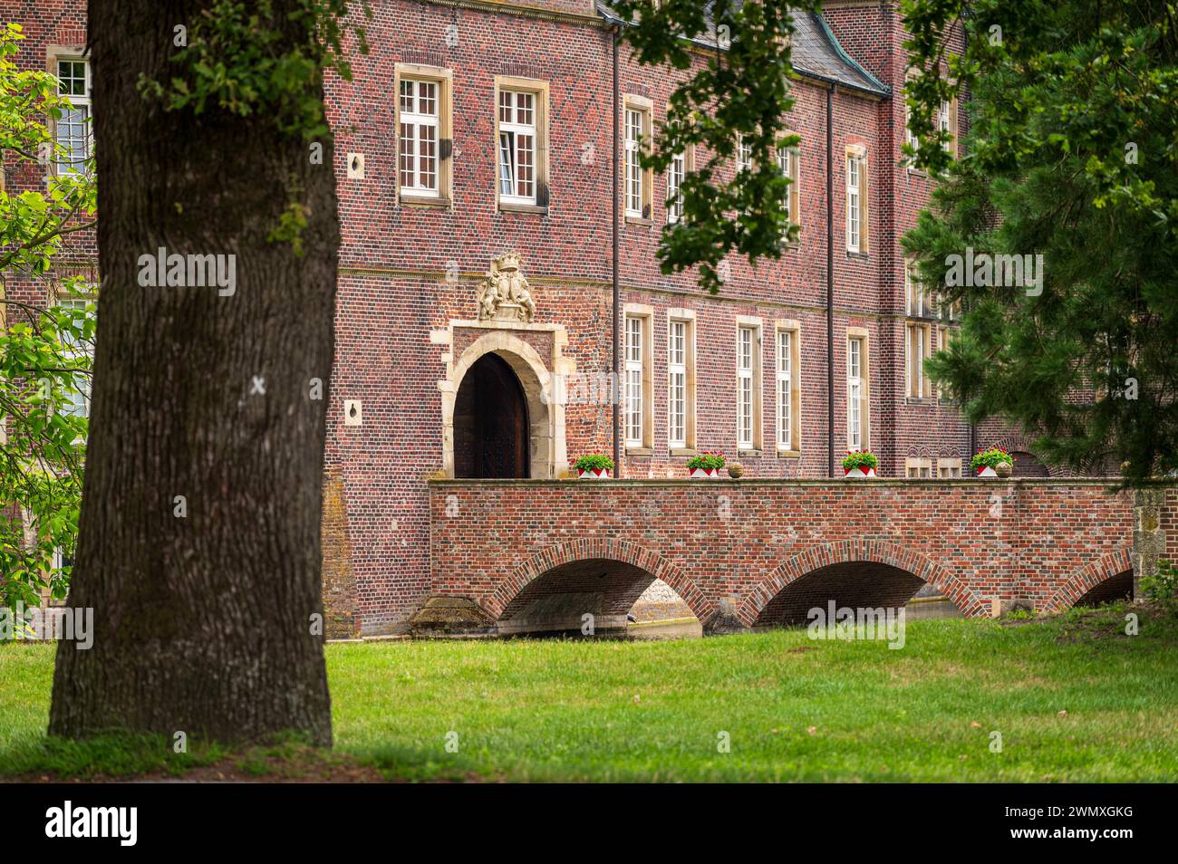 Brick castle with arched bridge, surrounded by trees and a lawn ...