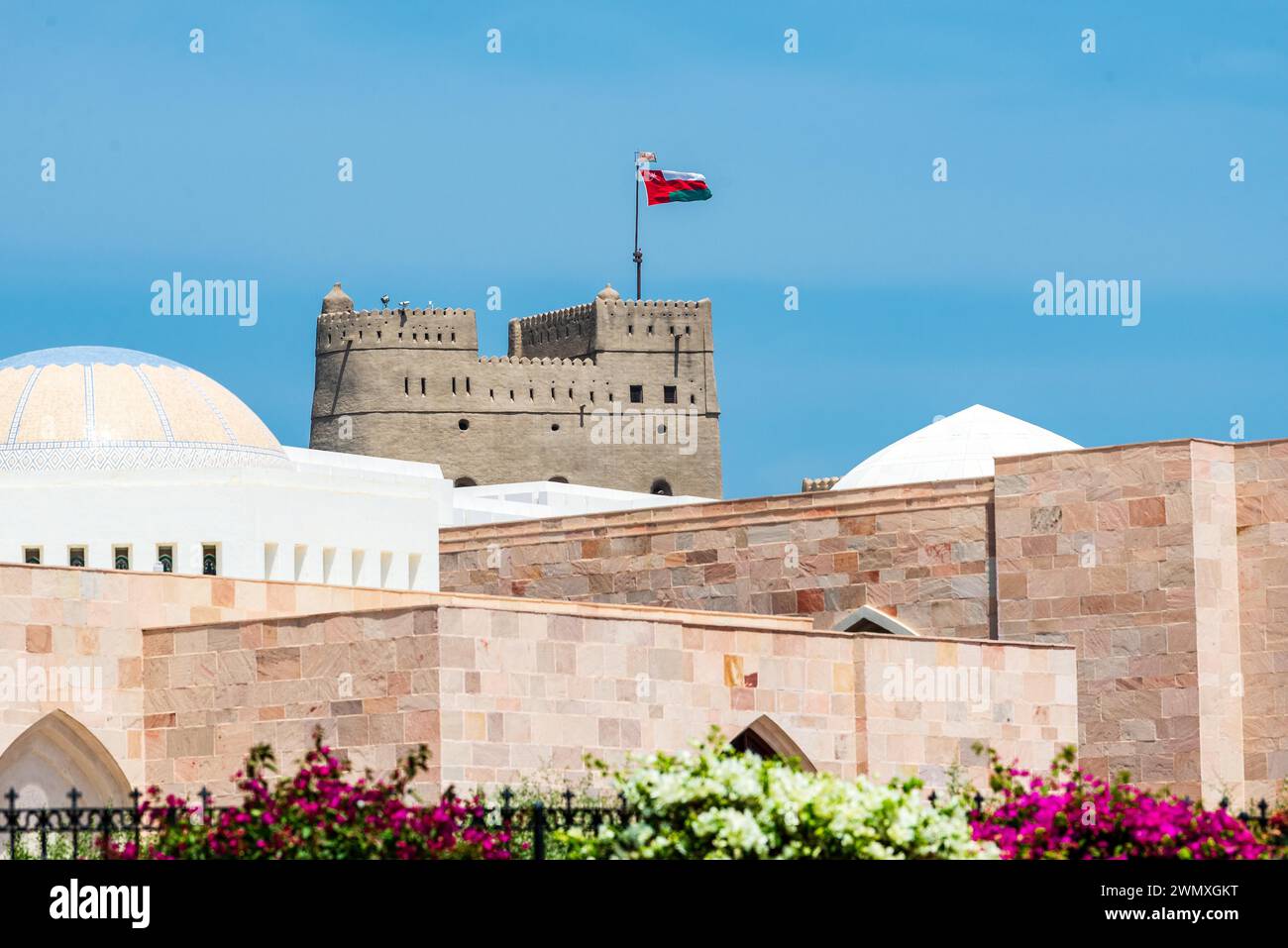 An old fortress with the Omani flag rises above pink stone buildings ...