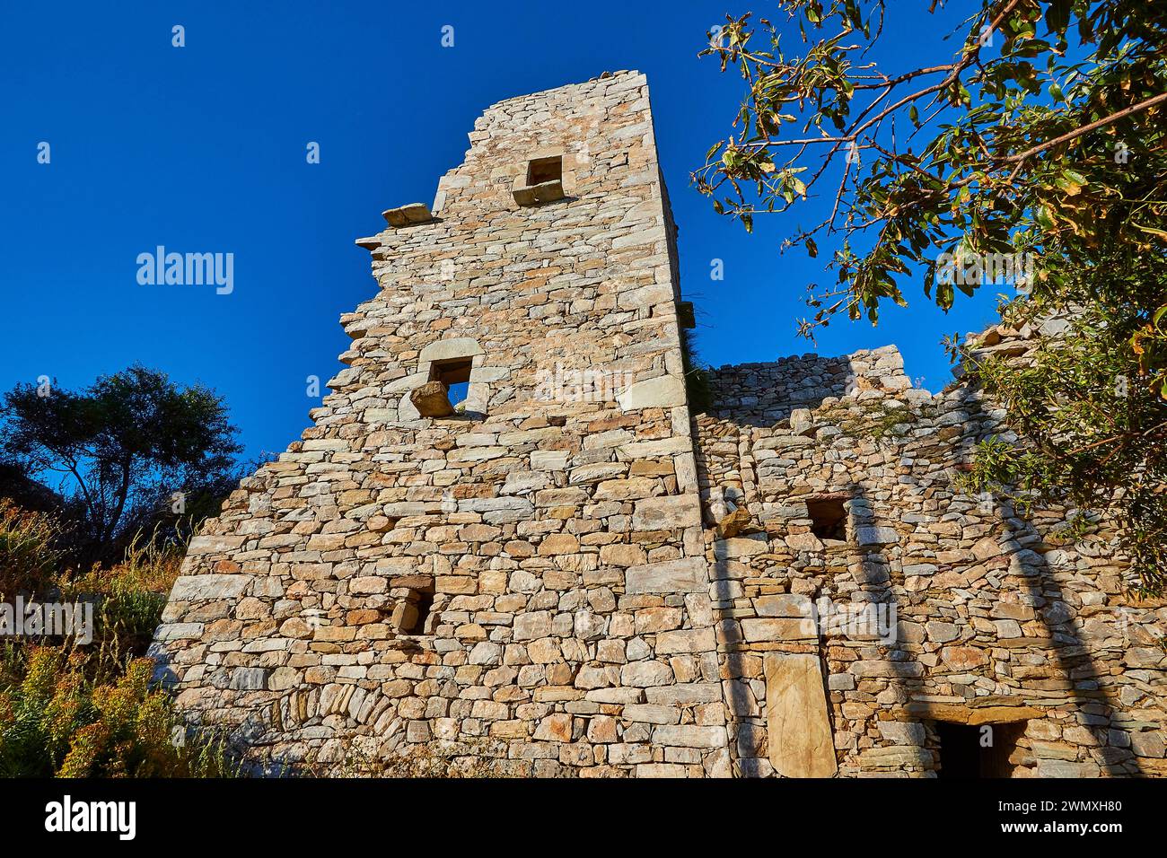 Stone walls of an old half-ruined tower against a blue sky, Vathi ...
