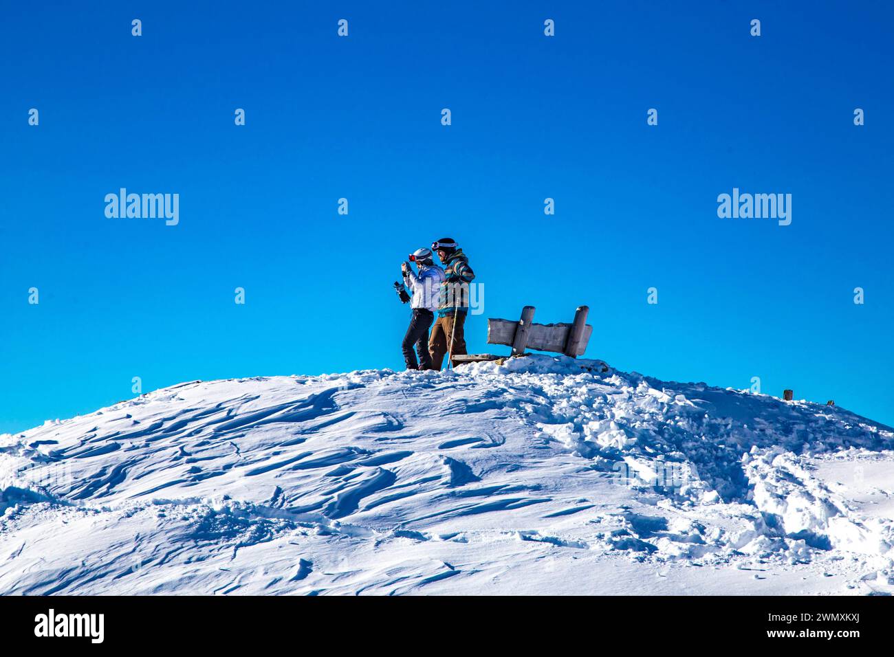 Two skiers take a photo at the summit in front of the descent, mountain ...