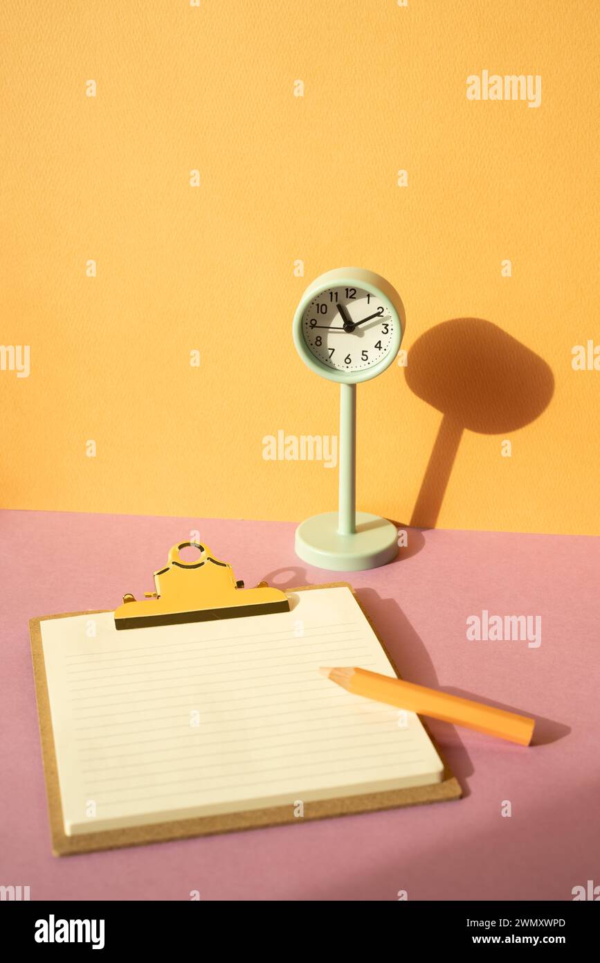 Clipboard and colored pencil, clock on pink desk. orange wall ...