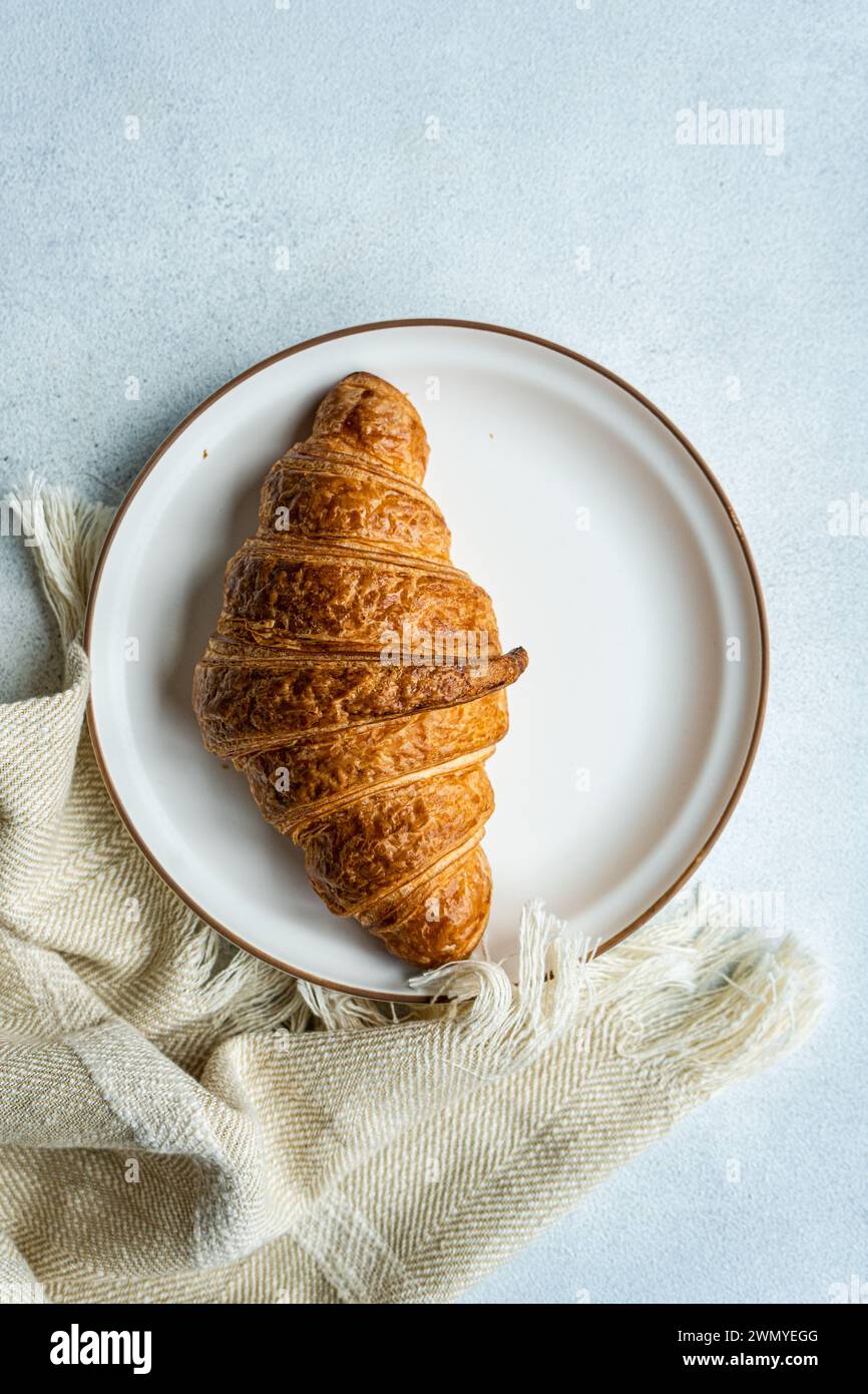 Top view of single croissant on a round plate, resting on a hessian ...