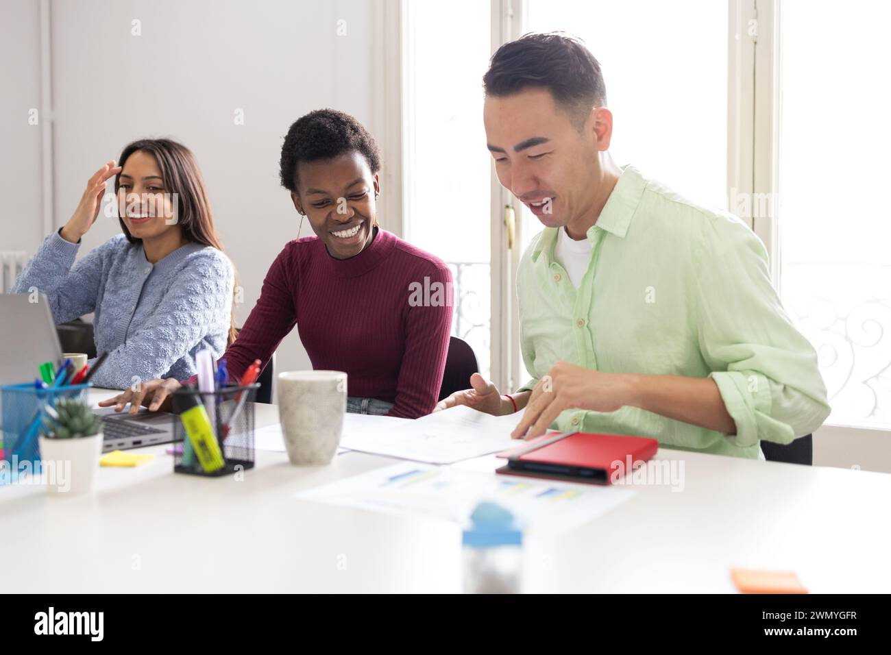 Three colleagues laughing together during a meeting in a well-lit ...