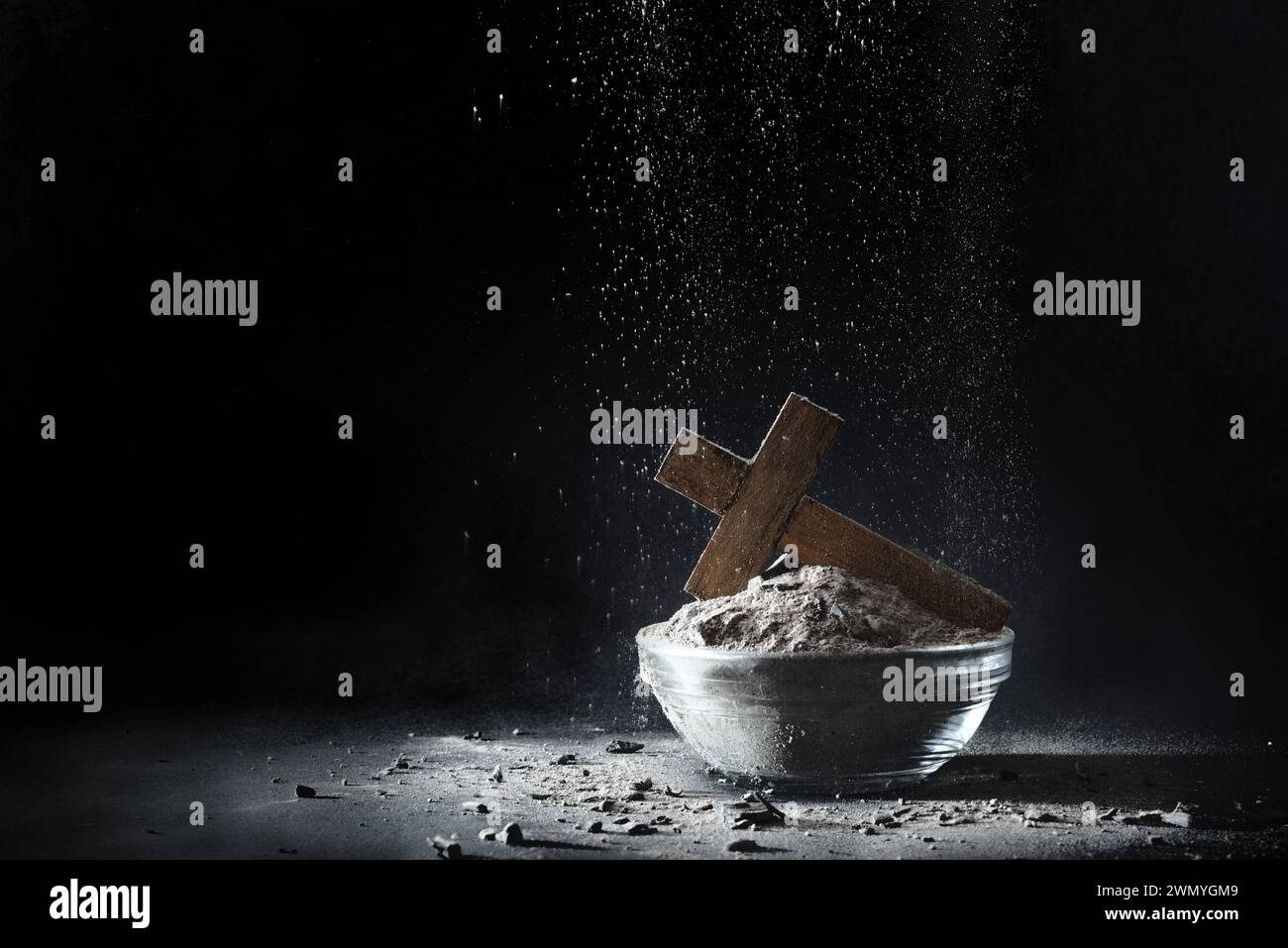 Cross on glass bowl full of ashes on table and dark background and ash ...