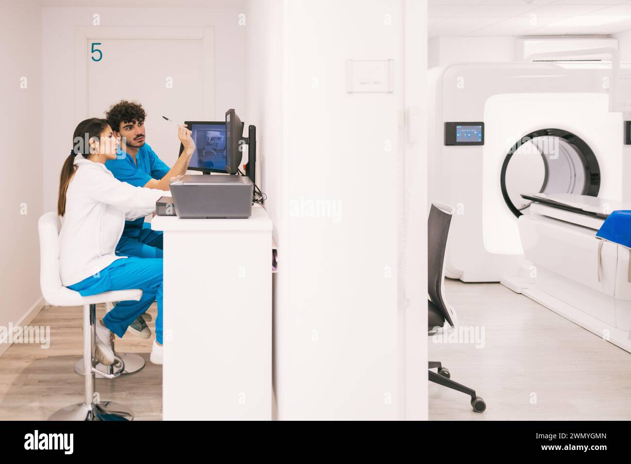 Two healthcare workers operate a magnetic resonance imaging (MRI ...