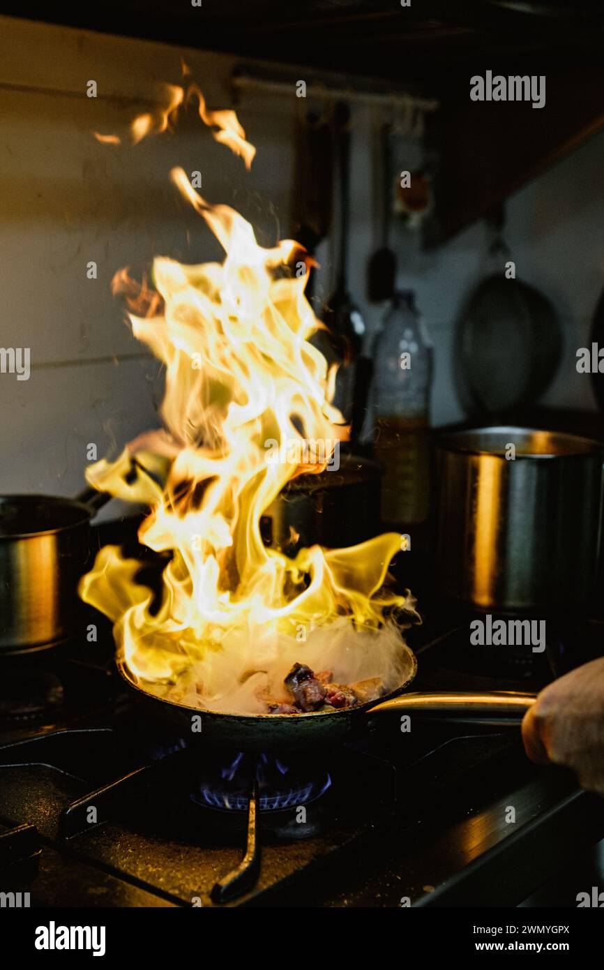 A dramatic shot of a skillet on a stove with a blazing fire engulfing ...