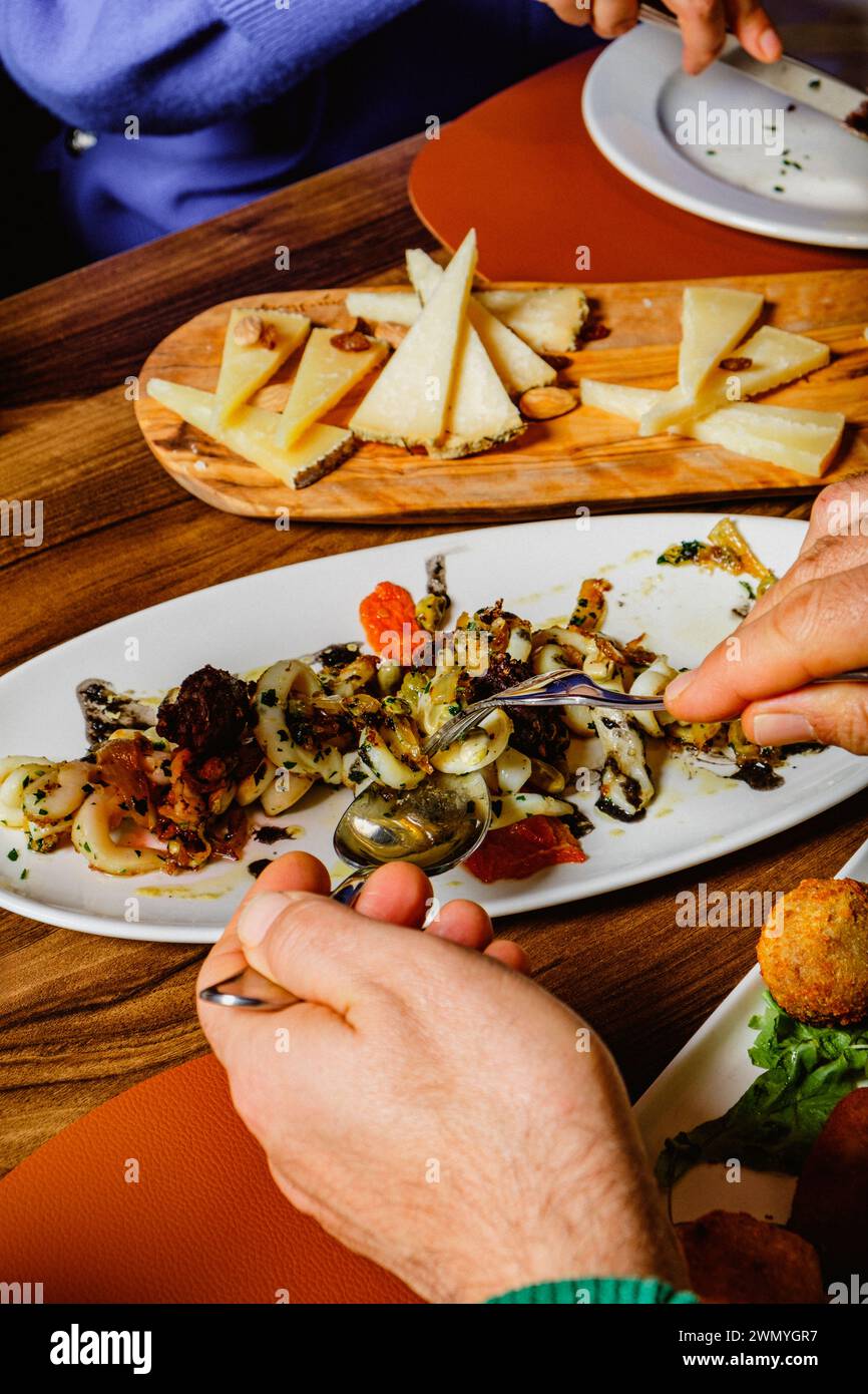 A person serving gourmet pasta from a shared plate, with a cheese ...