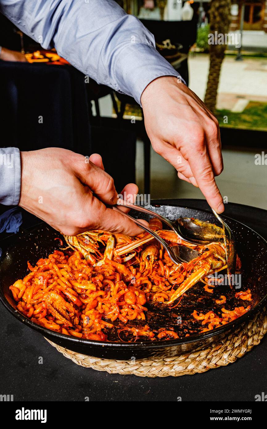 A person serves a sumptuous seafood pasta dish from a large pan at an ...