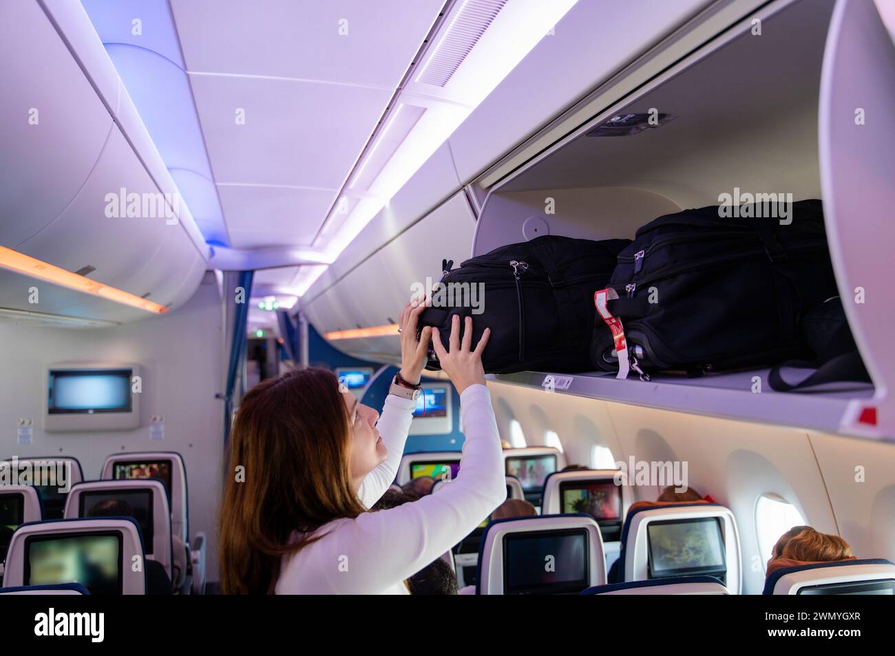 A woman is placing her bag into the overhead storage compartment on an ...