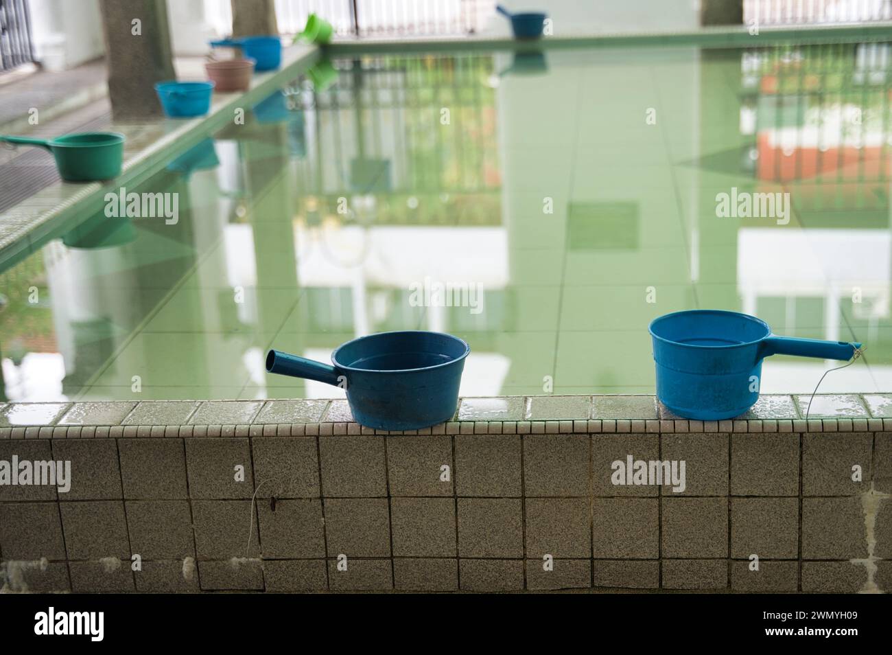 Two blue plastic water scoops rest on a tiled edge at the side of a ...