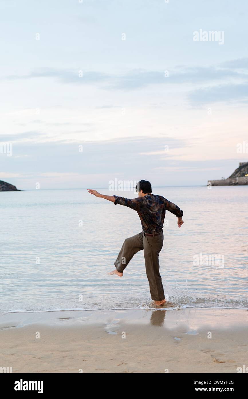 Man balancing playfully on one leg at the beach with outstretched arms ...