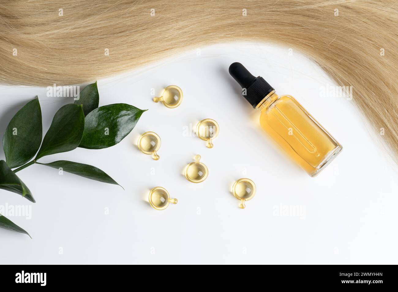 Long blonde hair flows beside a bottle of hair oil with droplets and ...