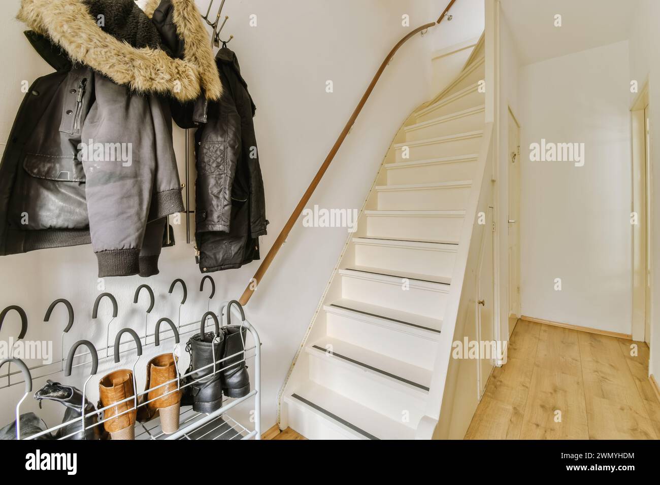 A well-organized home entrance featuring a white staircase, a clothing ...