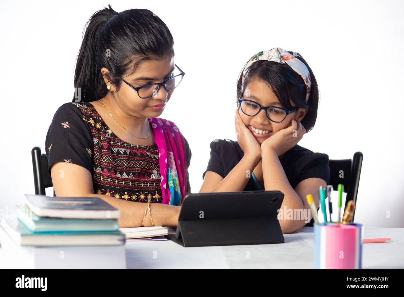 An Indian girl student studying with tablet besides her mother on white ...