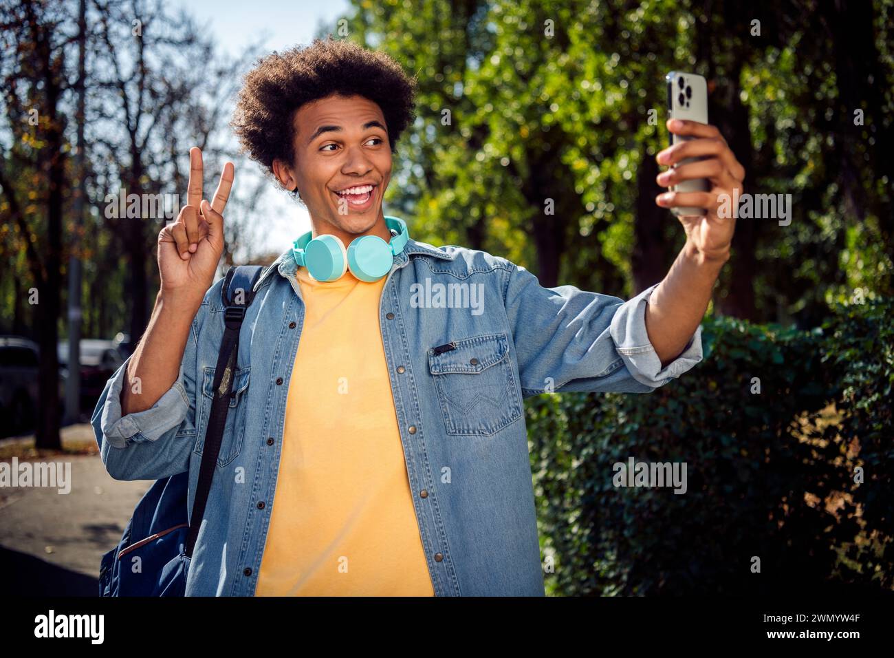 Photo of positive funky guy wear denim jacket earphones showing v-sign ...
