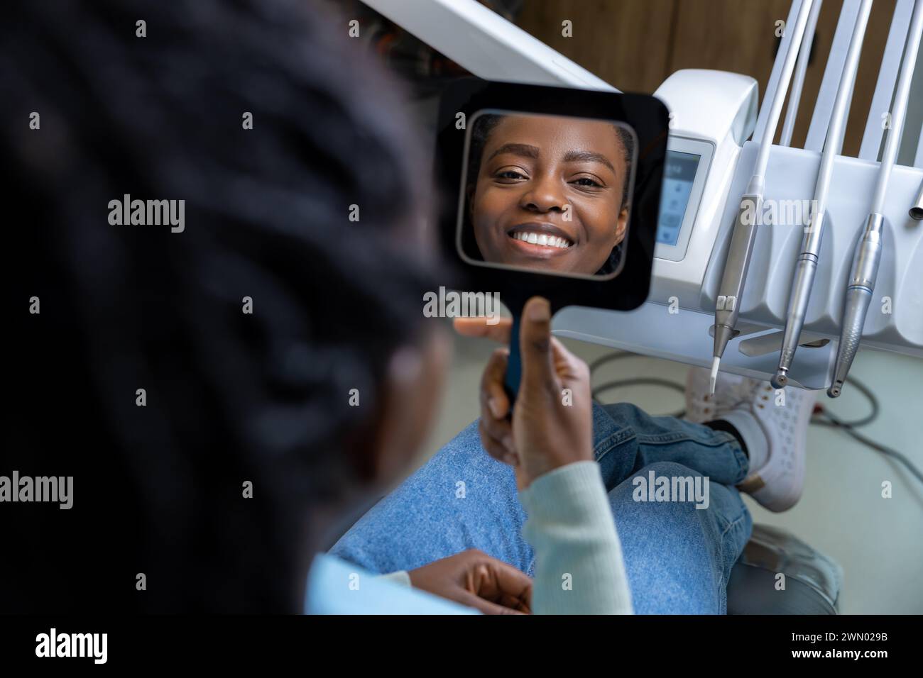 Happy multicultural female patient looking at mirror after dental ...