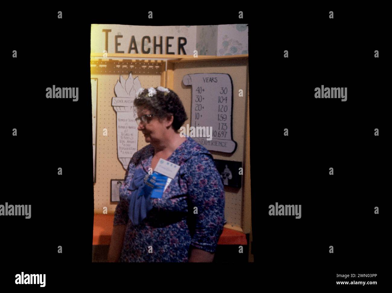 Woman wearing ribbon and NEA name tag standing by "Teacher" sign. Woman ...