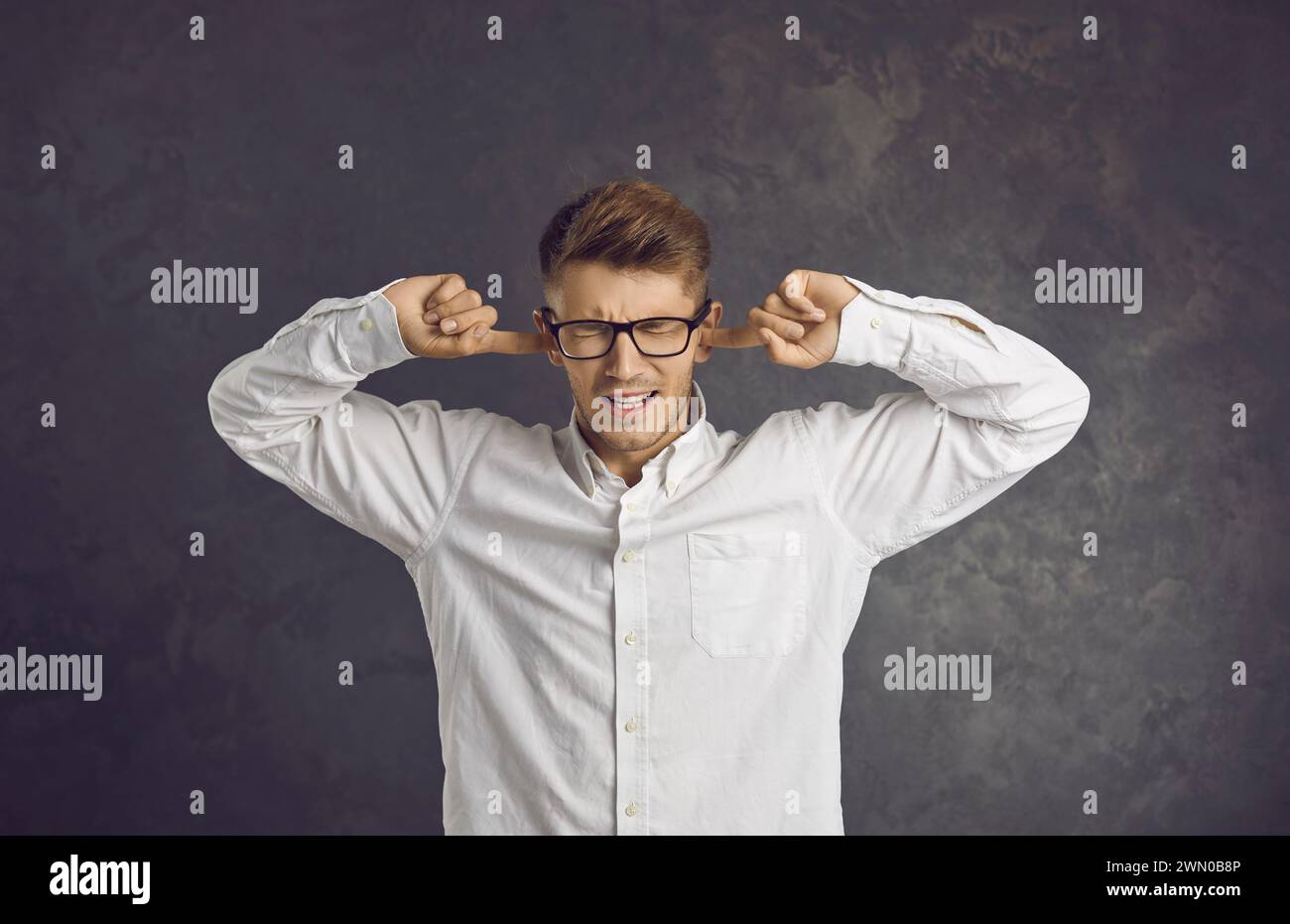 Portrait of young man trying to ignore loud noise and plugging ears ...